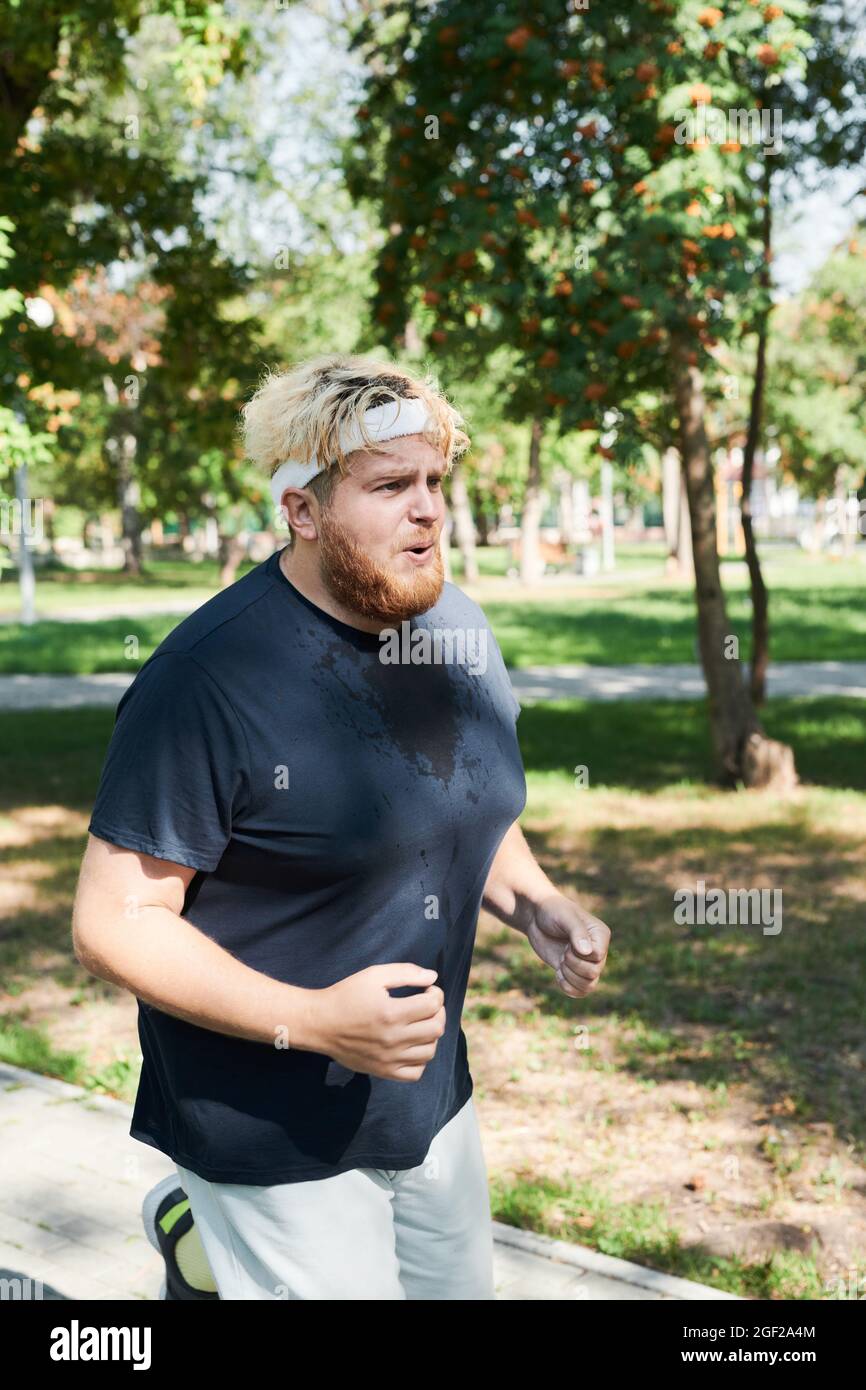 Young overweight man running outdoors in the park during his sport ...