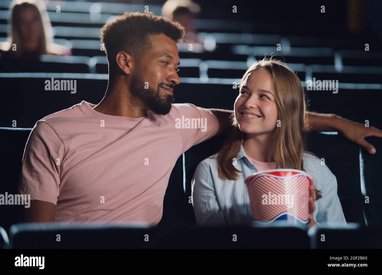 Front view of cheerful young couple in love in the cinema, watching ...