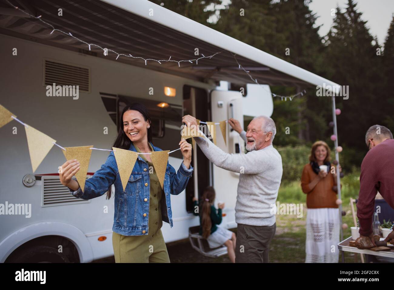 Multi-generation family preparing party by car outdoors in campsite ...