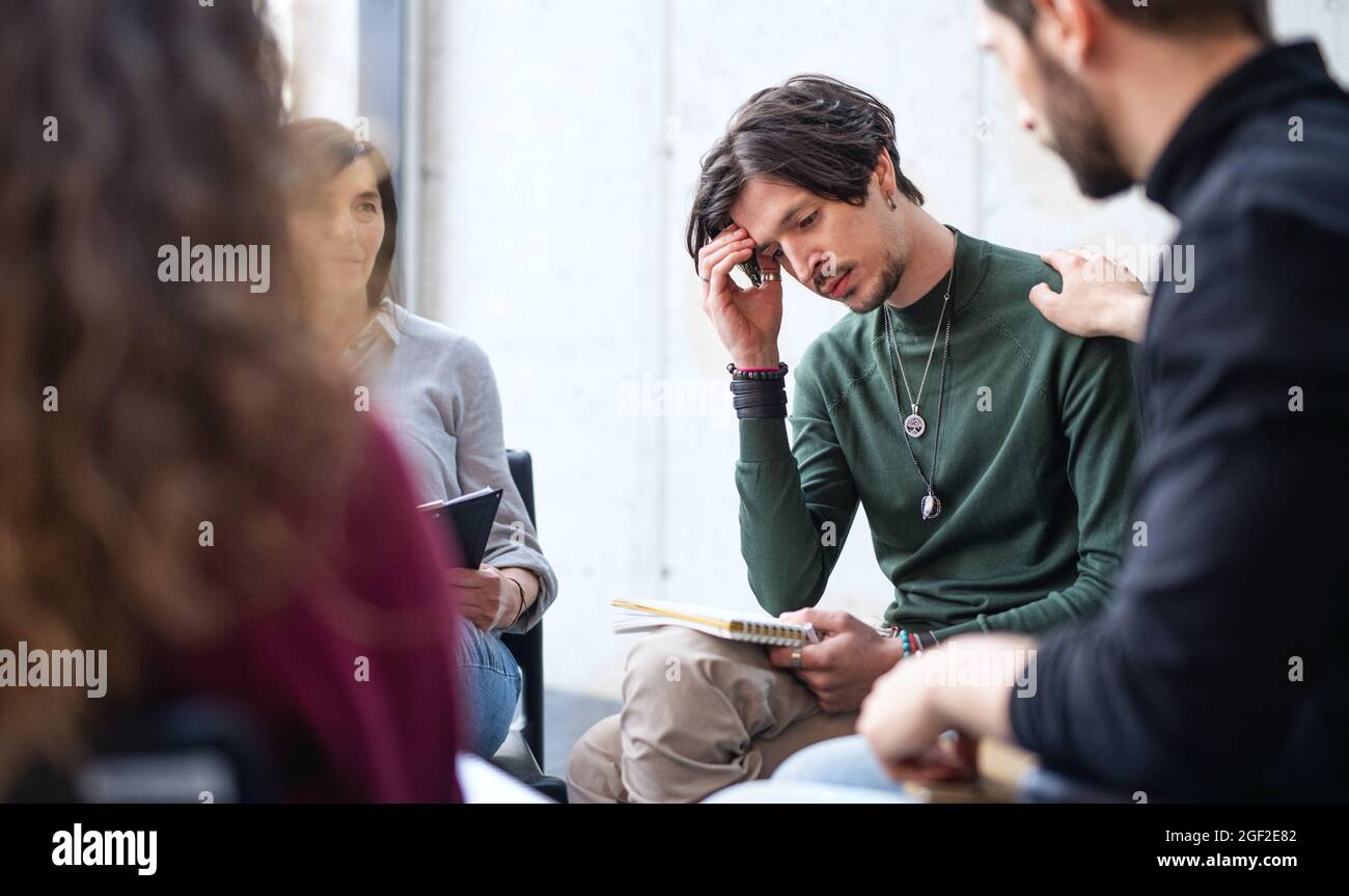 Sad and depressed man sitting in circle on group therapy, others ...
