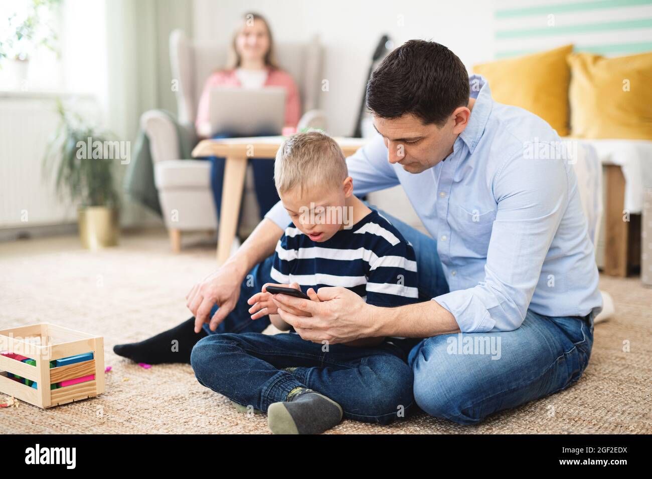 Father with happy down syndrome son indoors at home, using smartphone ...