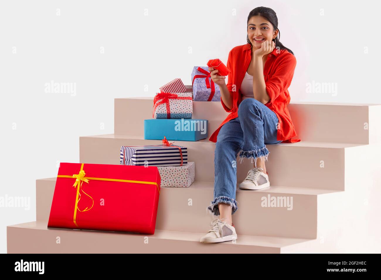 A young woman sitting on stairs with gift boxes in her hand and beside ...