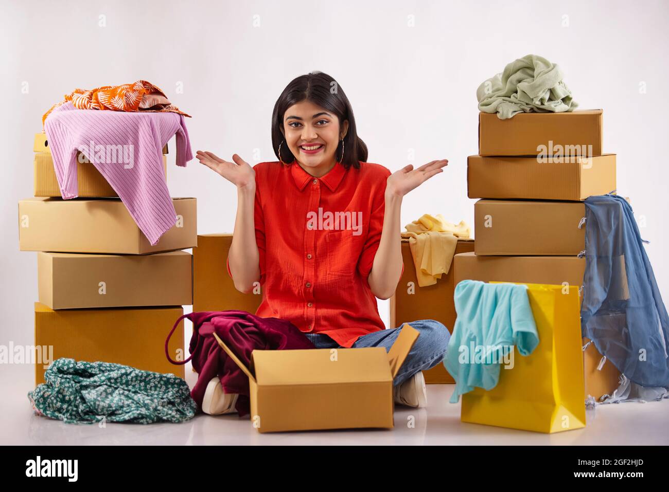 A young woman sitting amidst boxes, clothes and shoppingbags overjoyed ...