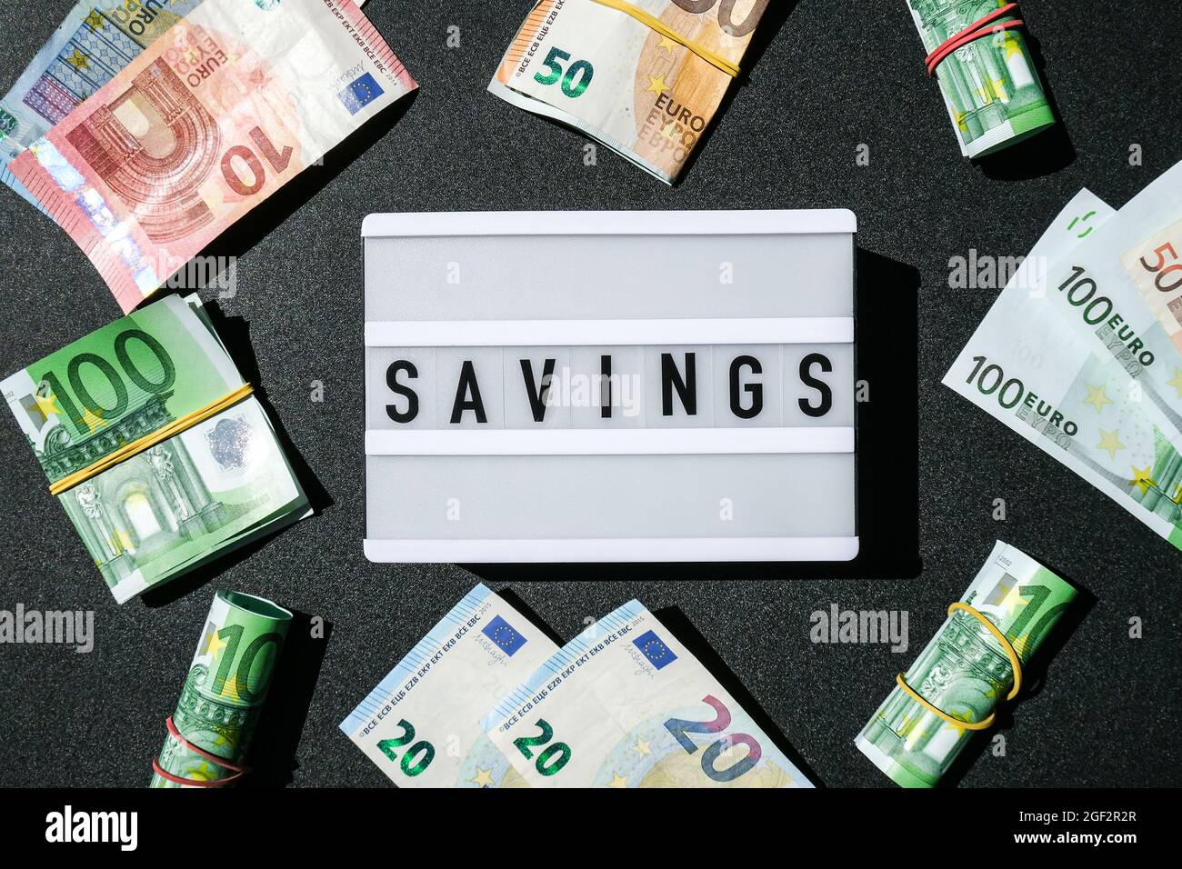 Lightbox board with word SAVINGS in black letters around Euro banknotes ...