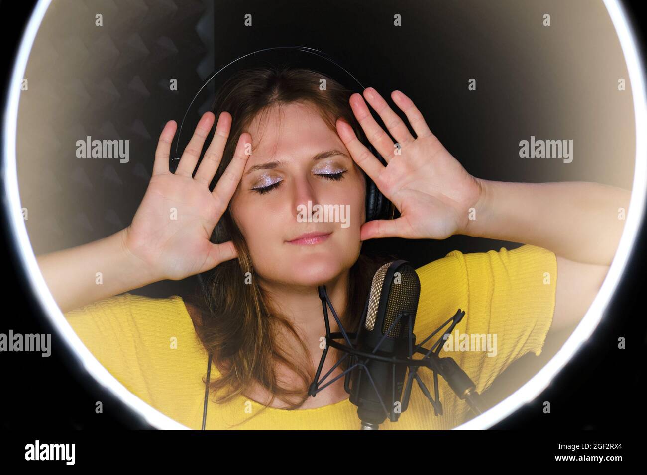 The woman sings at the recording Studio with her hands near her head ...