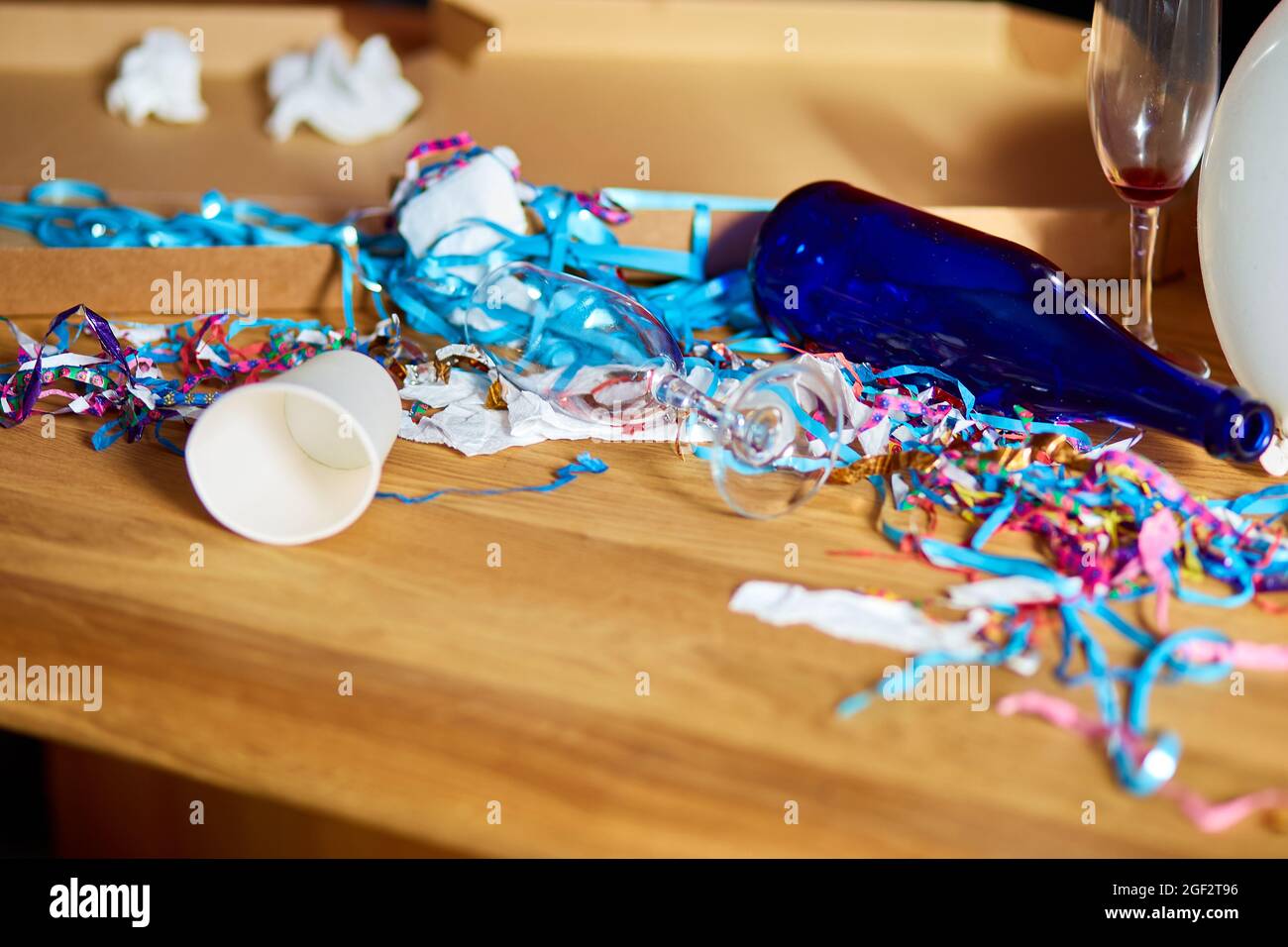 Messy wooden table with pizza box, empty blue bottles, wine glass and ...