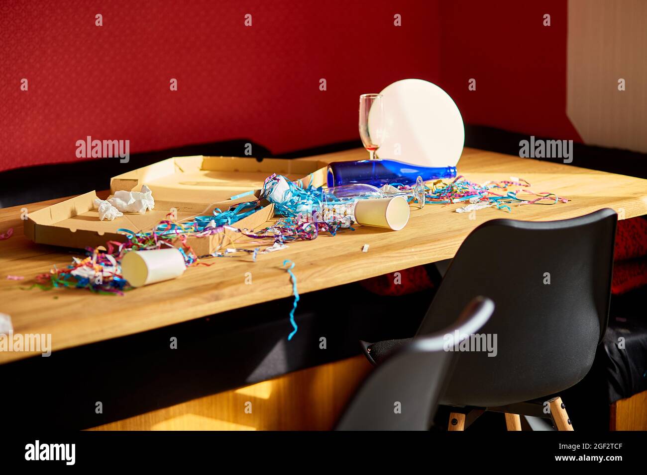 Messy wooden table with pizza box, empty blue bottles, wine glass and ...