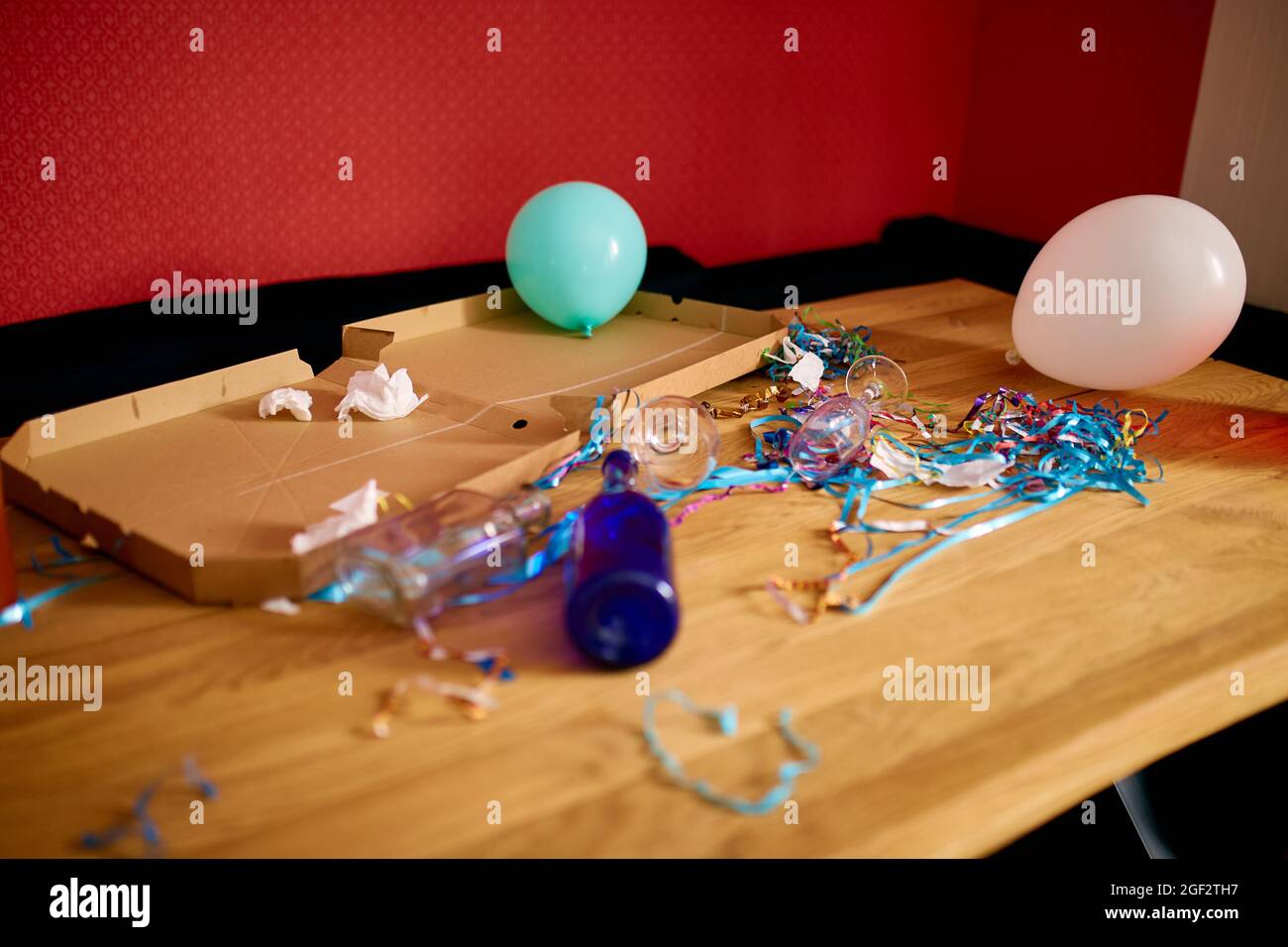 Messy wooden table with pizza box, empty blue bottles, wine glass and ...