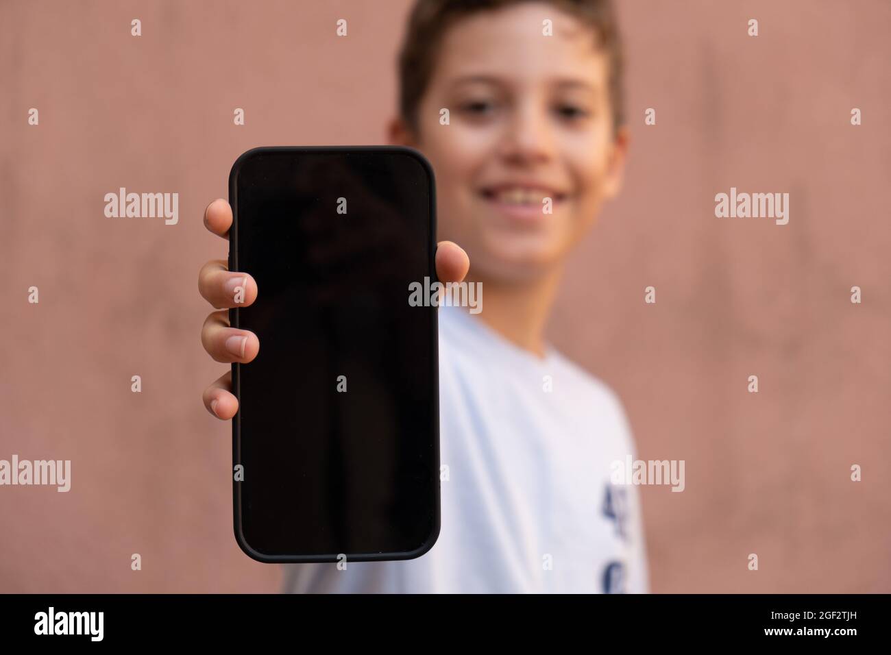 Cheerful little boy holding smart mobile phone with blank black display ...