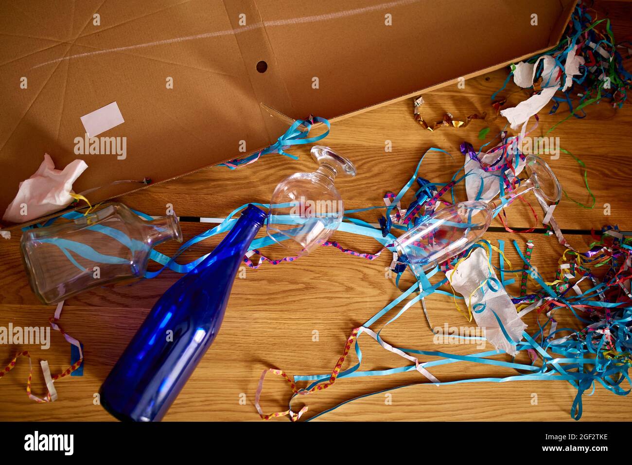 Messy wooden table with pizza box, empty blue bottles, wine glass and ...