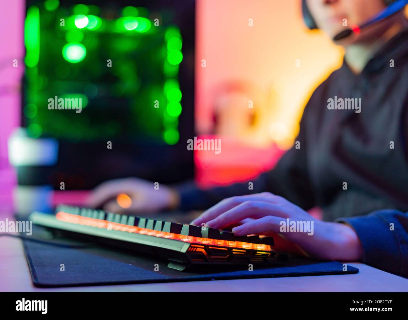 Unrecognizable young gamer with hands on illuminated keyboard in room ...