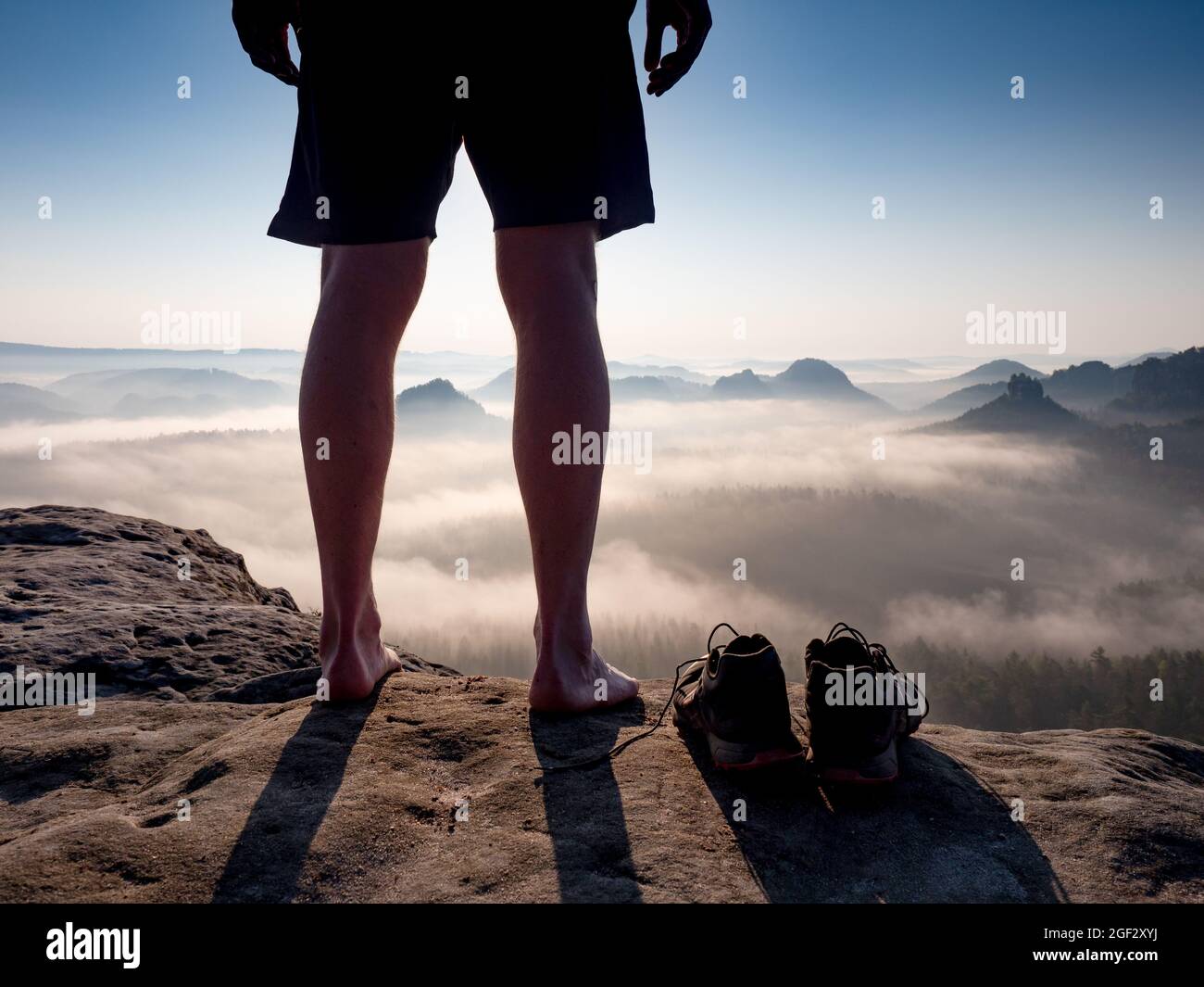 Slim male legs in strong backlight. Barefoot man hiker feet climbing on ...