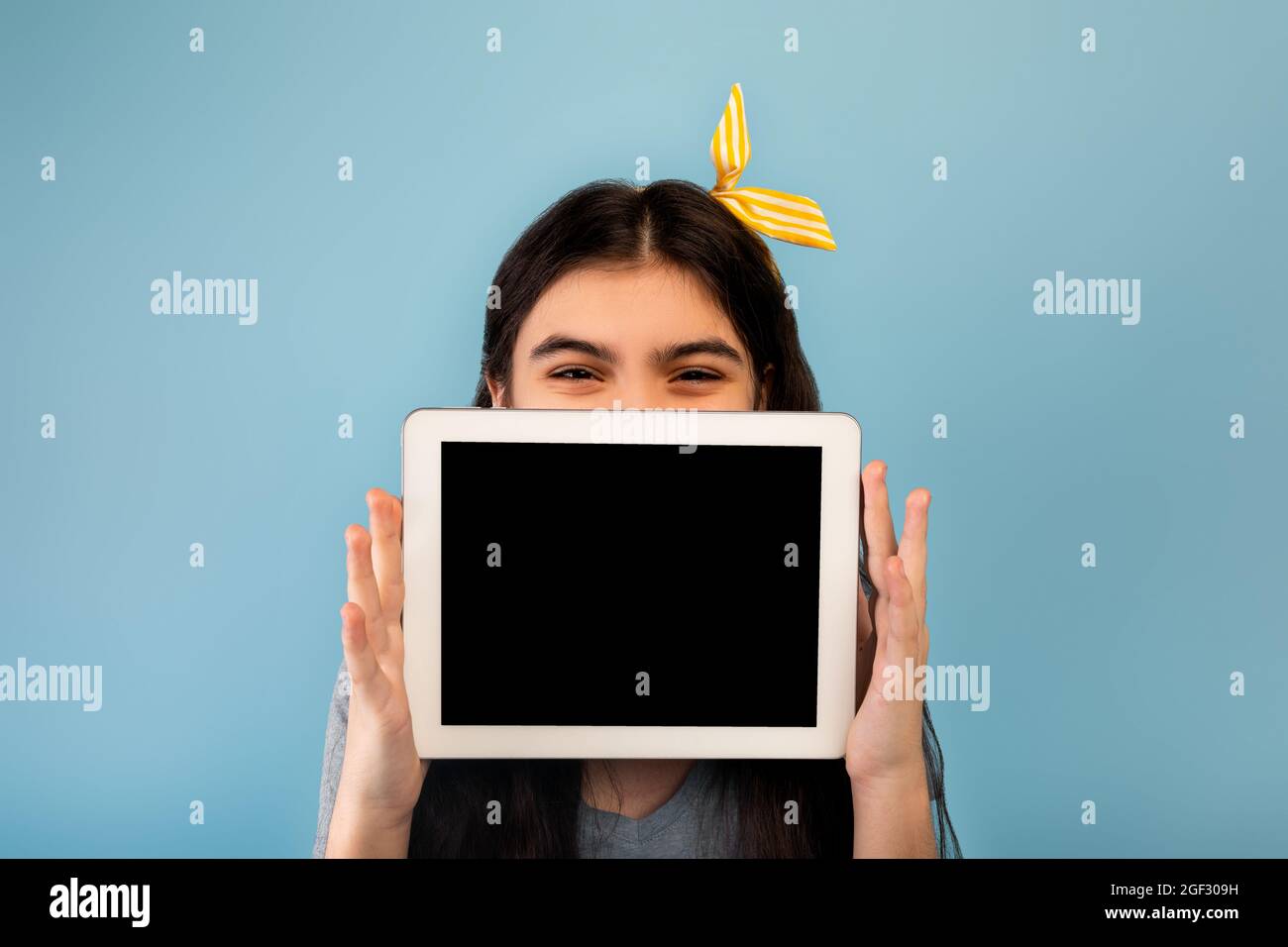 Indian teen girl hiding behind tablet computer with empty screen on ...