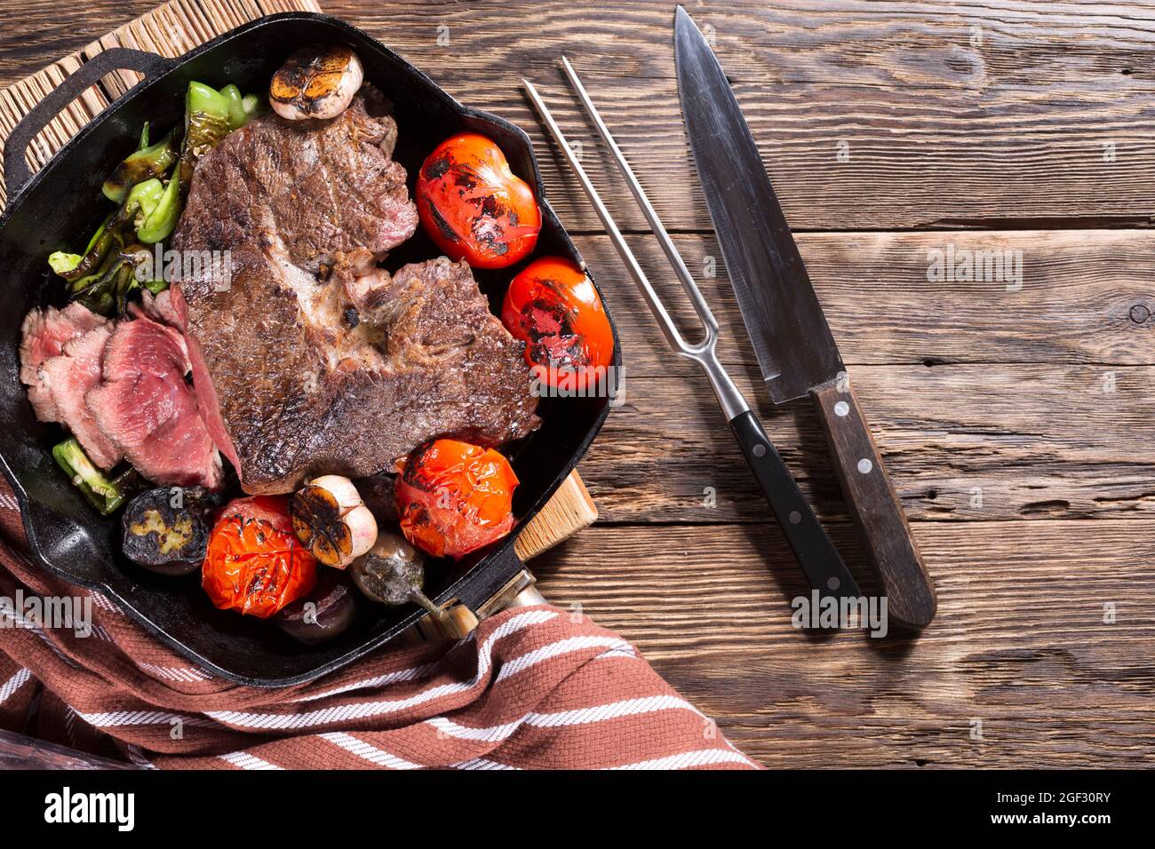 A piece of meat grilled in a cast-iron pan with vegetables, closeup ...