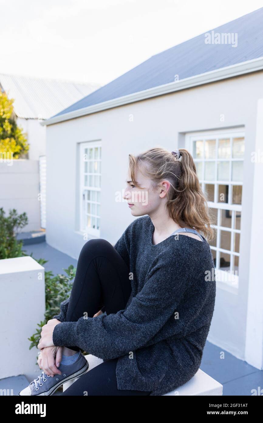 Teenage girl sitting outside a house on a low wall, waiting Stock Photo ...