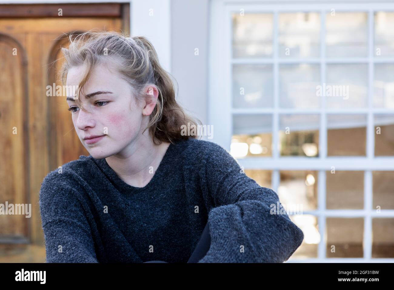 A teenage girl sitting outside alone, looking bored Stock Photo - Alamy