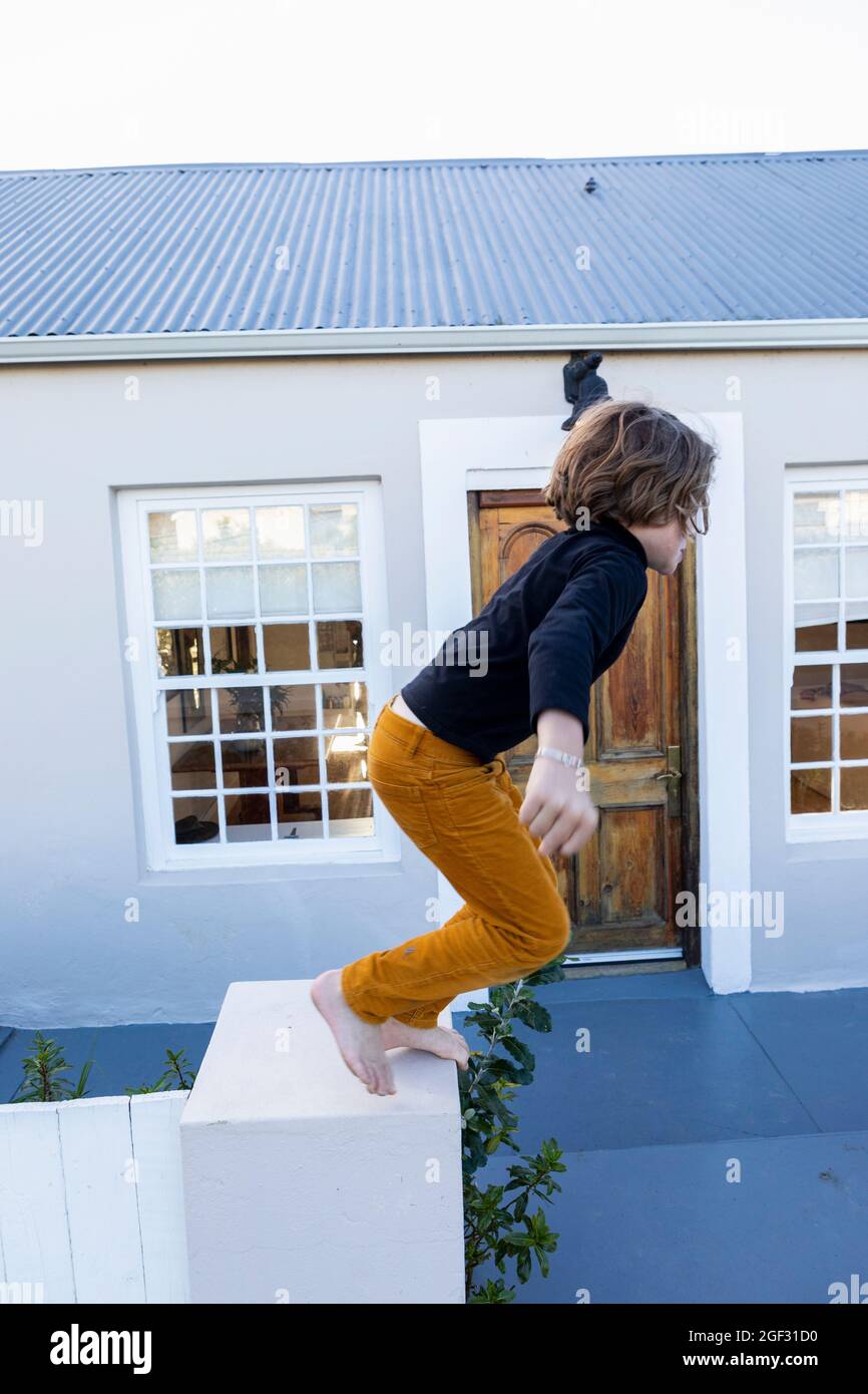 Young boy jumping off a low wall outside a house Stock Photo - Alamy