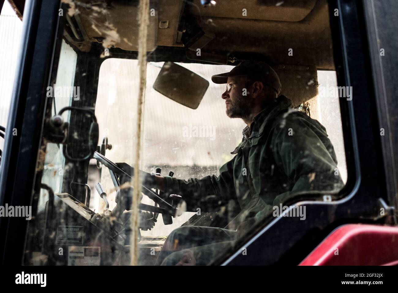 Side view of farmer sitting in the cabin of a tractor Stock Photo - Alamy