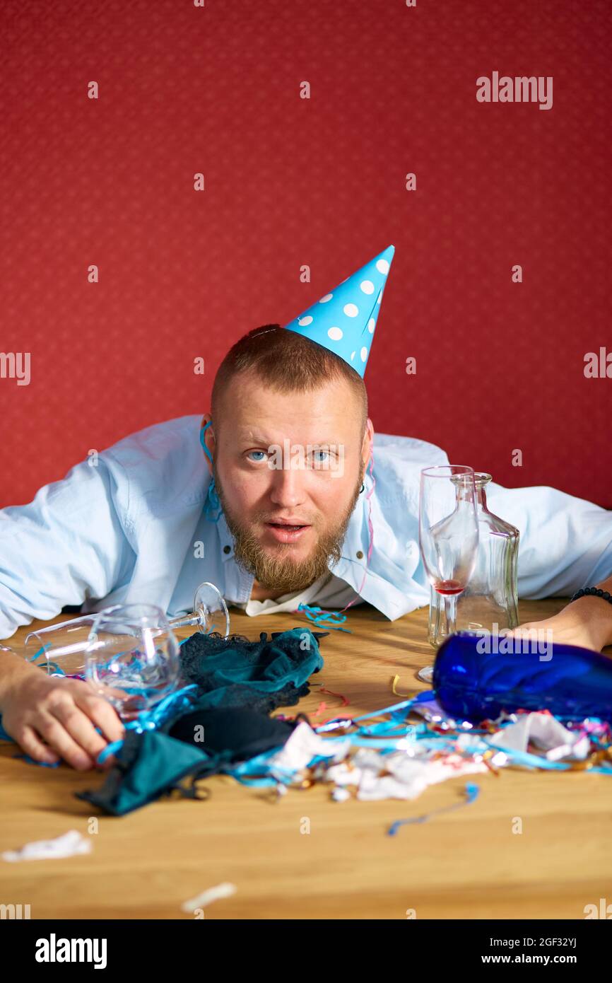 Tired man at table with blue cap in messy room after birthday party ...