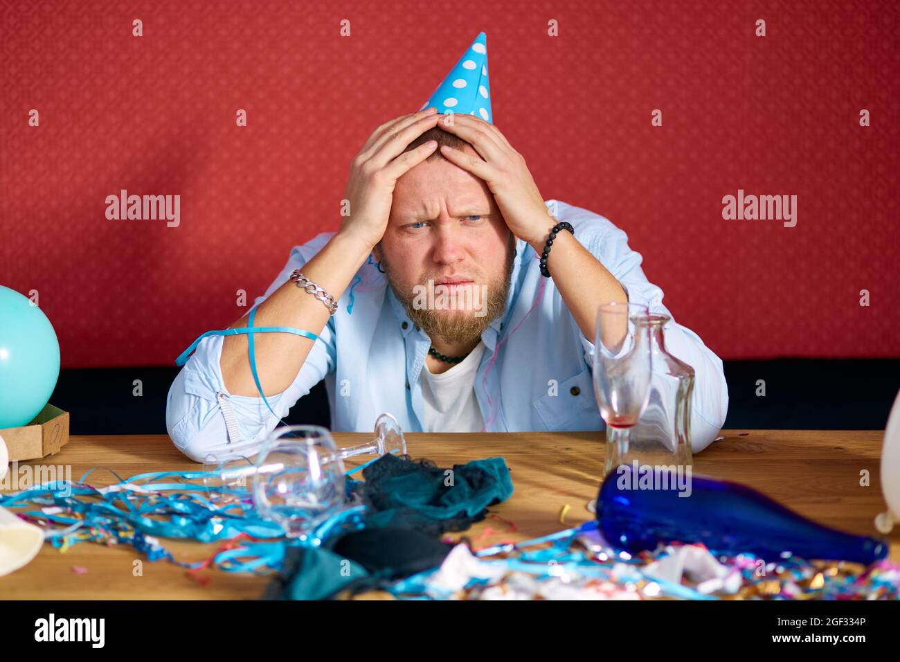 Man suffering from hangover at table with blue cap in messy room after ...