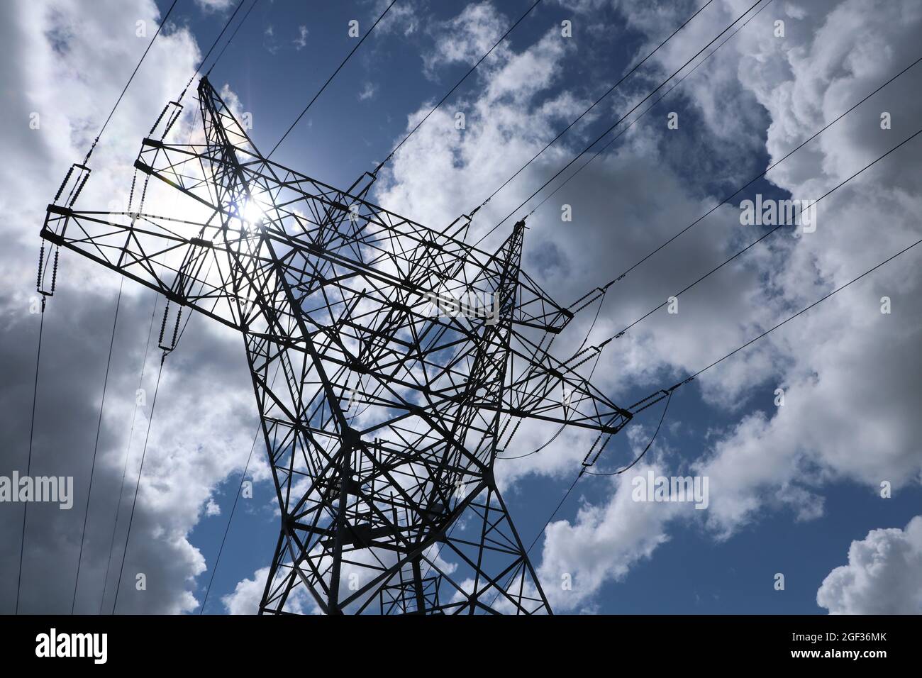 Power pylon against sky with sunshine through clouds, low angle view ...