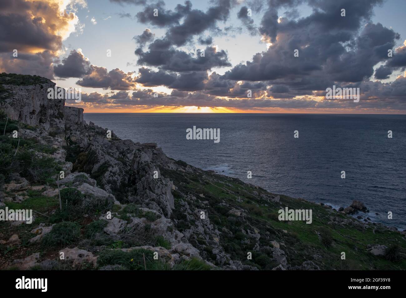 A peaceful cloudy sunset, as seen from on top of a sloping cliff along ...