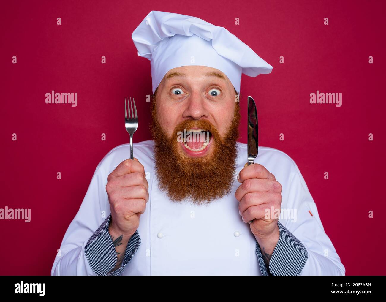 amazed chef with beard and red apron holds cutlery in hand Stock Photo ...