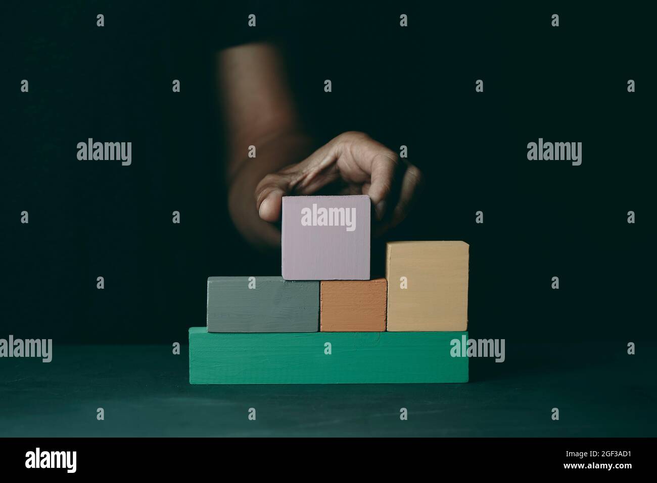 a caucasian man builds a structure with some wooden toy blocks of ...