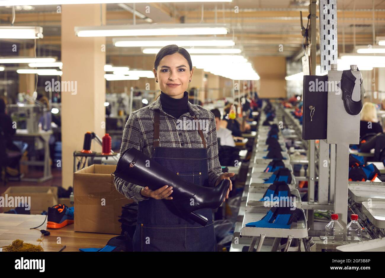 Happy female shoe factory worker holding a women's heeled boot from the ...