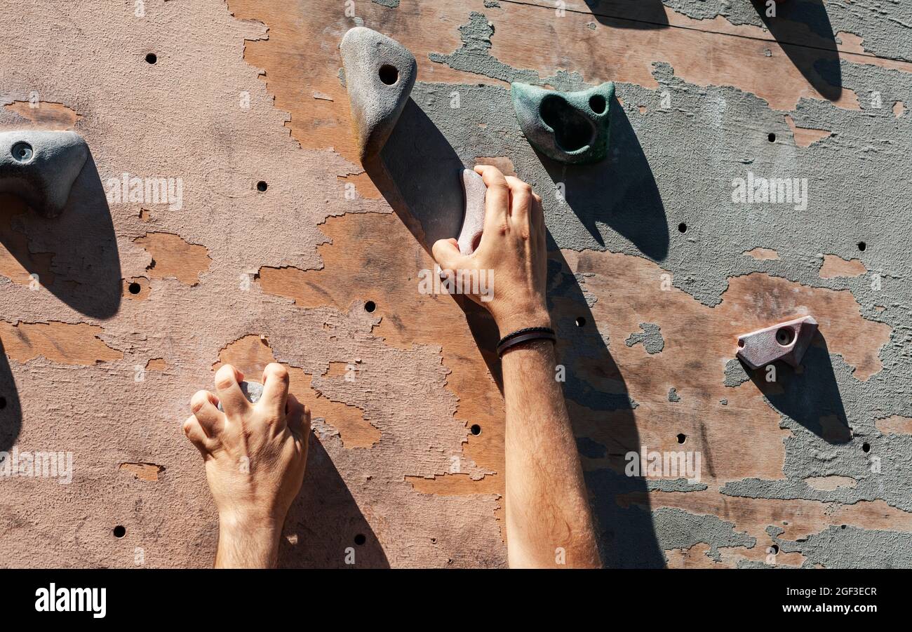 Close-up photo of male hands gripping climbing holds on worn wall ...