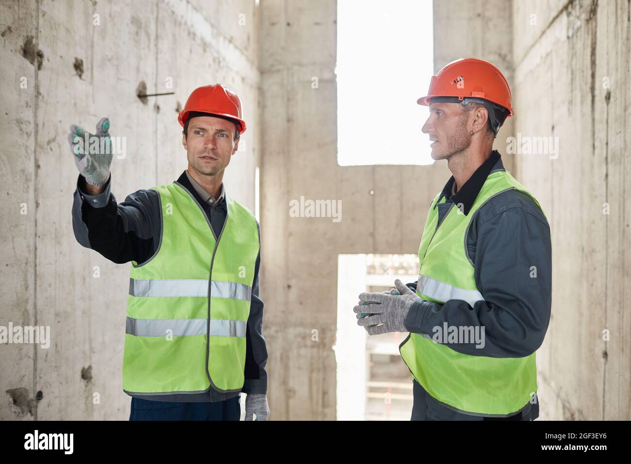 Waist up portrait of two engineers at construction site pointing away ...
