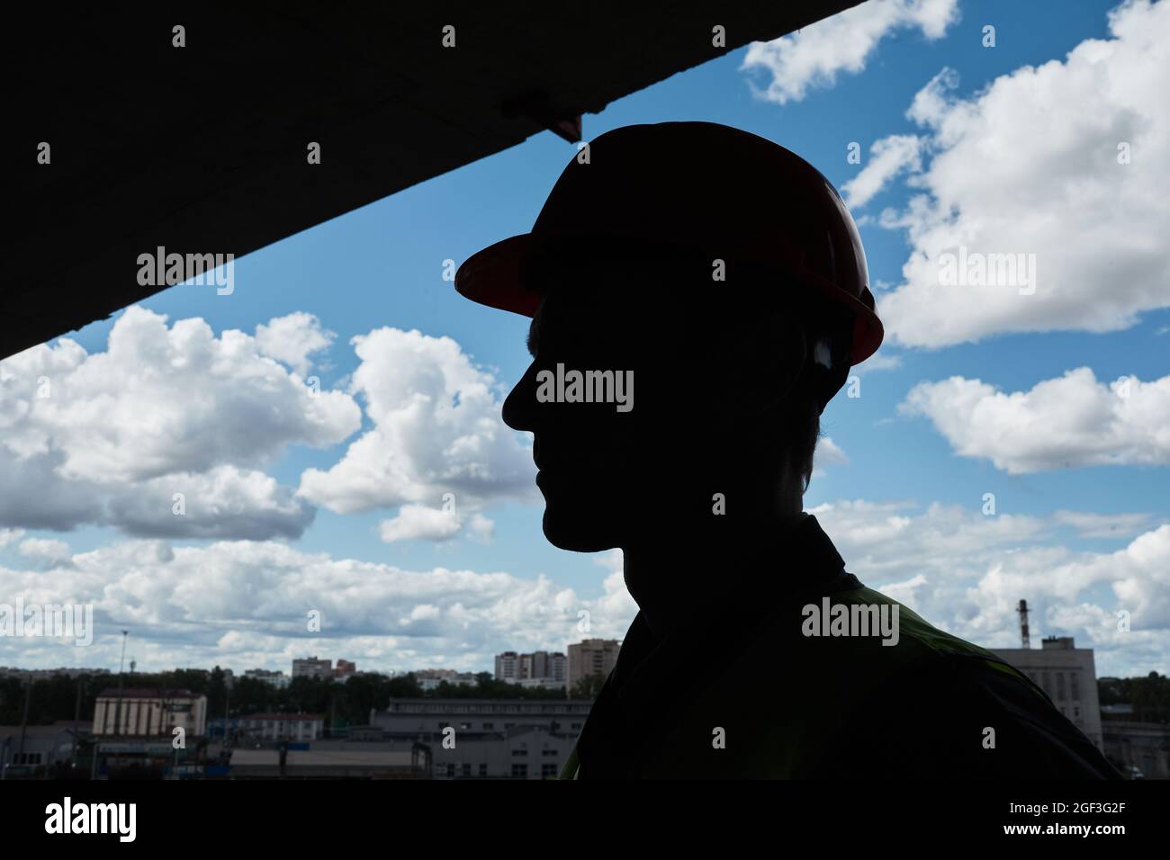 Backlit profile view at unrecognizable worker wearing hardhat against ...