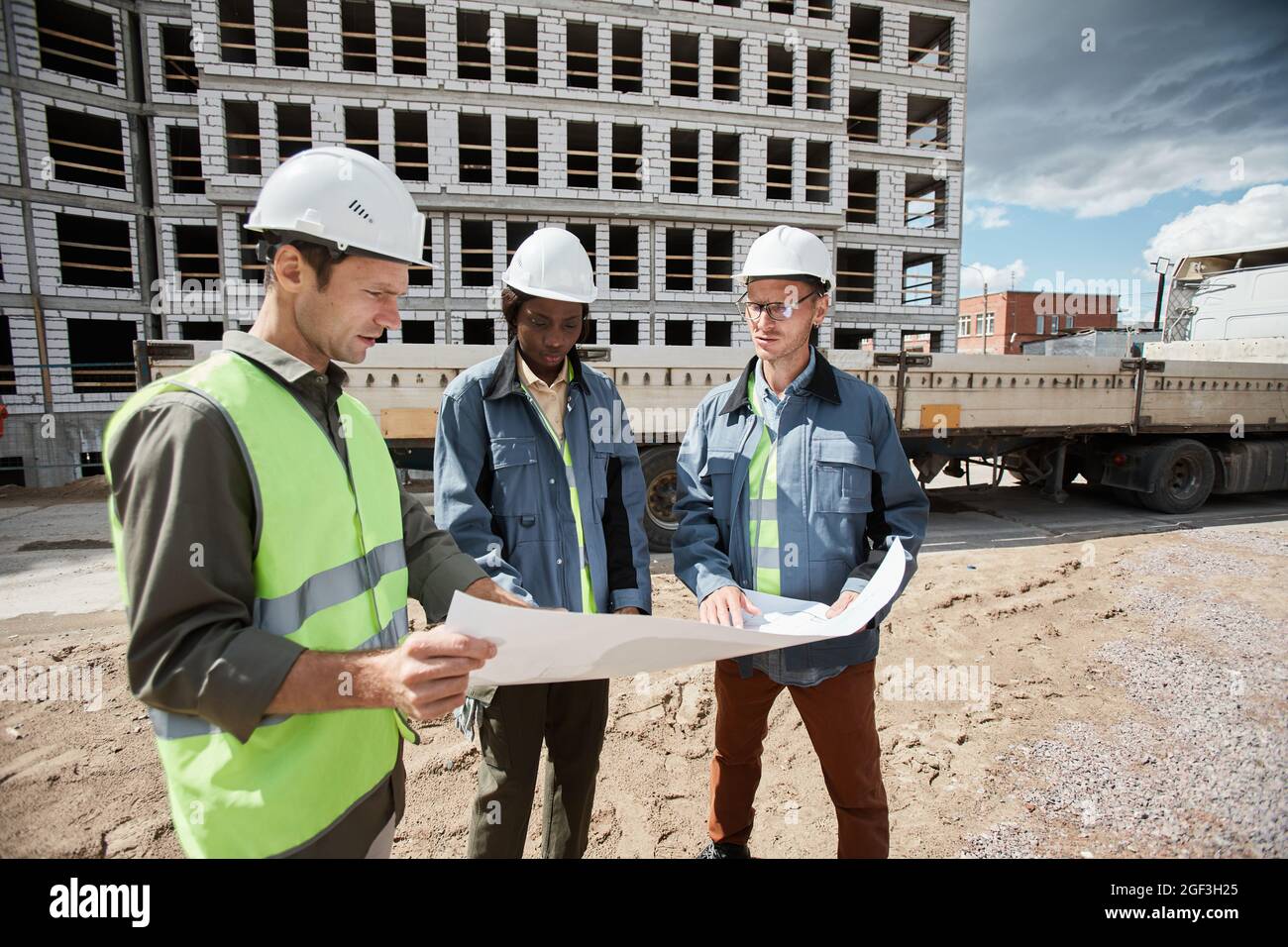 Diverse group of engineers discussing floor plans at construction site ...