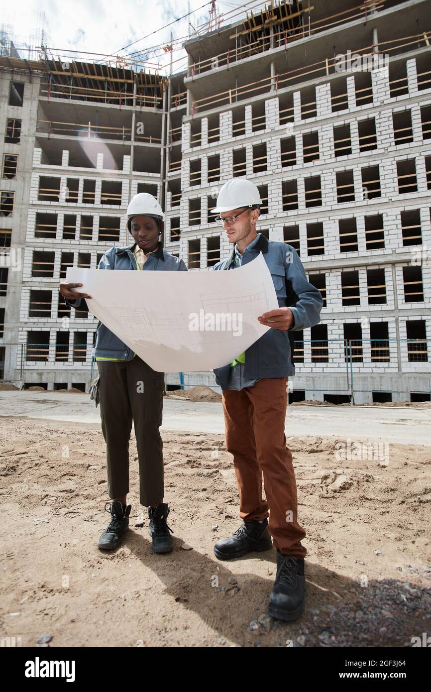 Full length portrait of two engineers discussing floor plans at ...