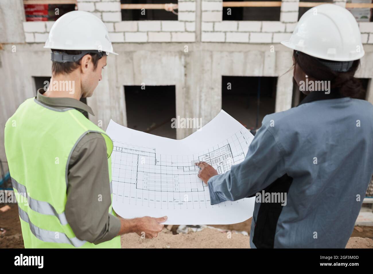 Back view portrait of two workers discussing floor plans at ...