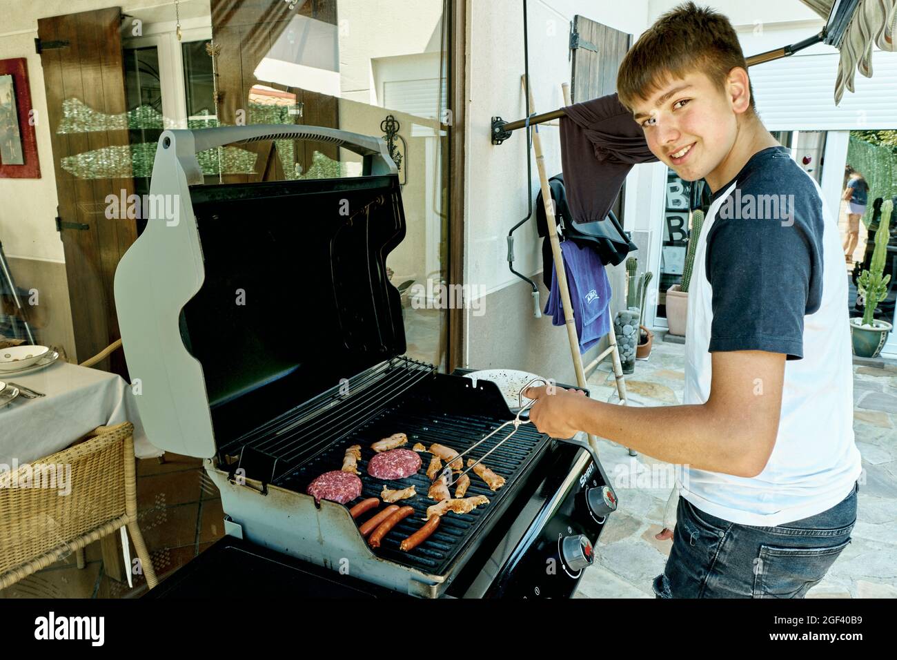 Portrait of a young caucasian boy grilling meat on the barbecue in the ...