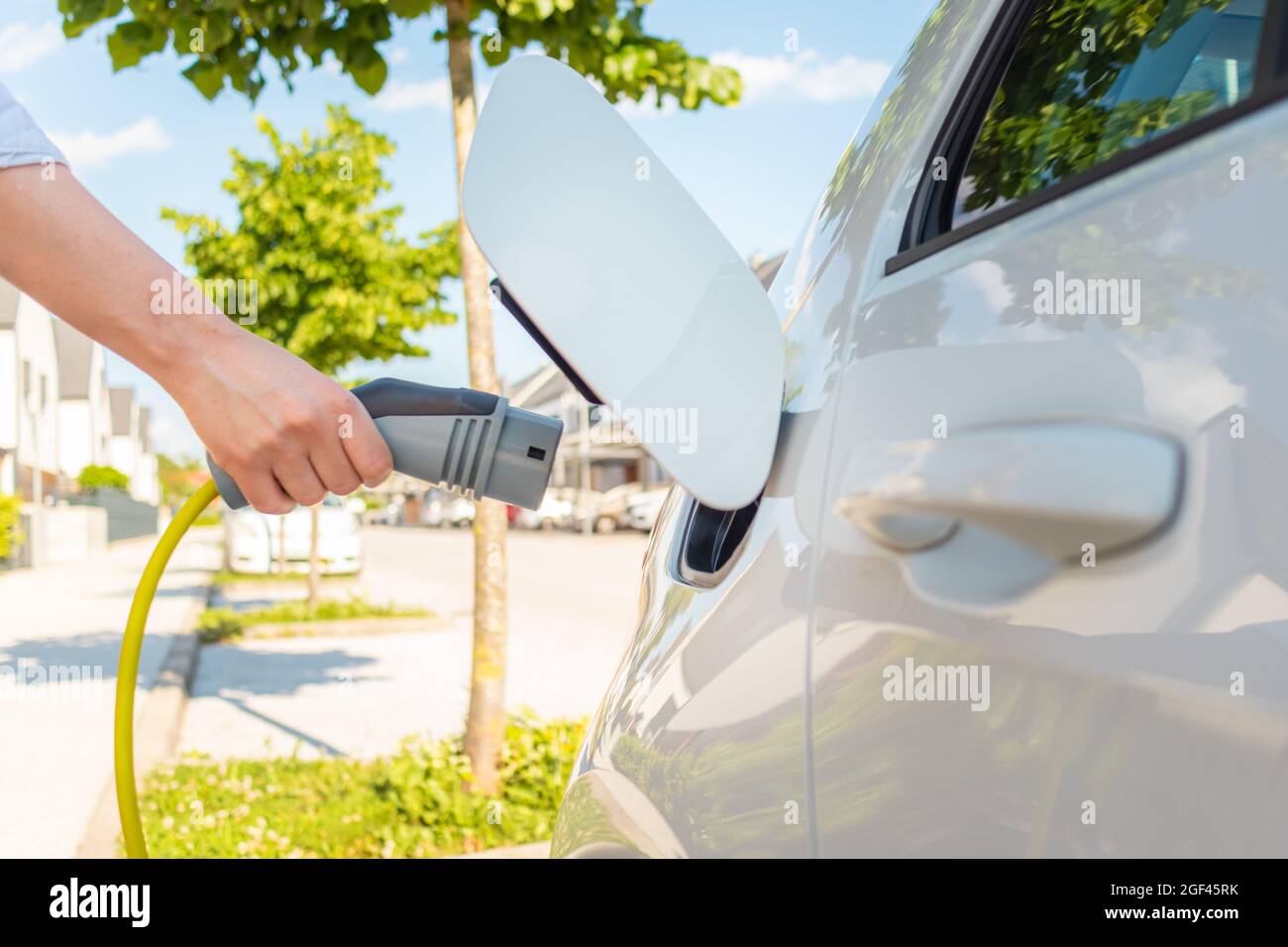 Female hands opening an electric car charging socket cap and plugging ...