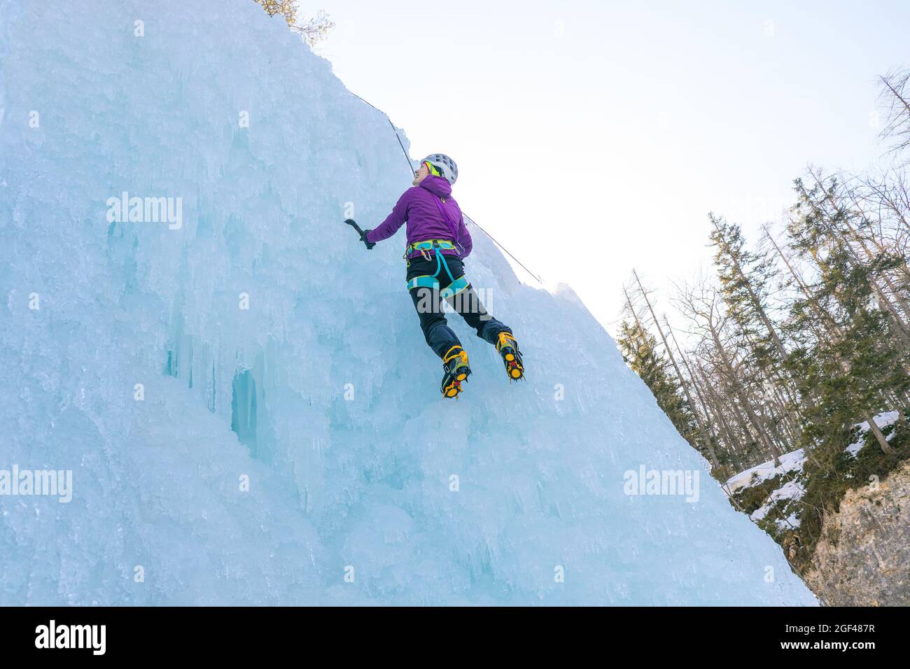 Female ice climber in traction position, swinging ice axes overhead and ...