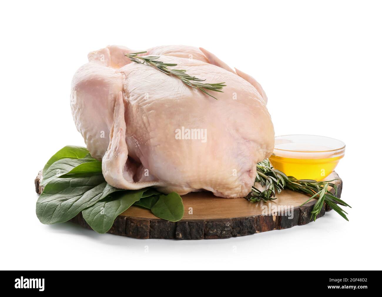 Board with whole raw chicken, oil, rosemary and spinach on white ...