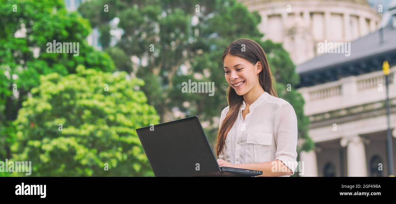 Asian business woman working on laptop computer outside in city park ...
