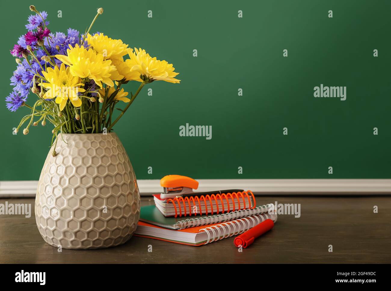 Vase with beautiful flowers and stationery on table in classroom ...