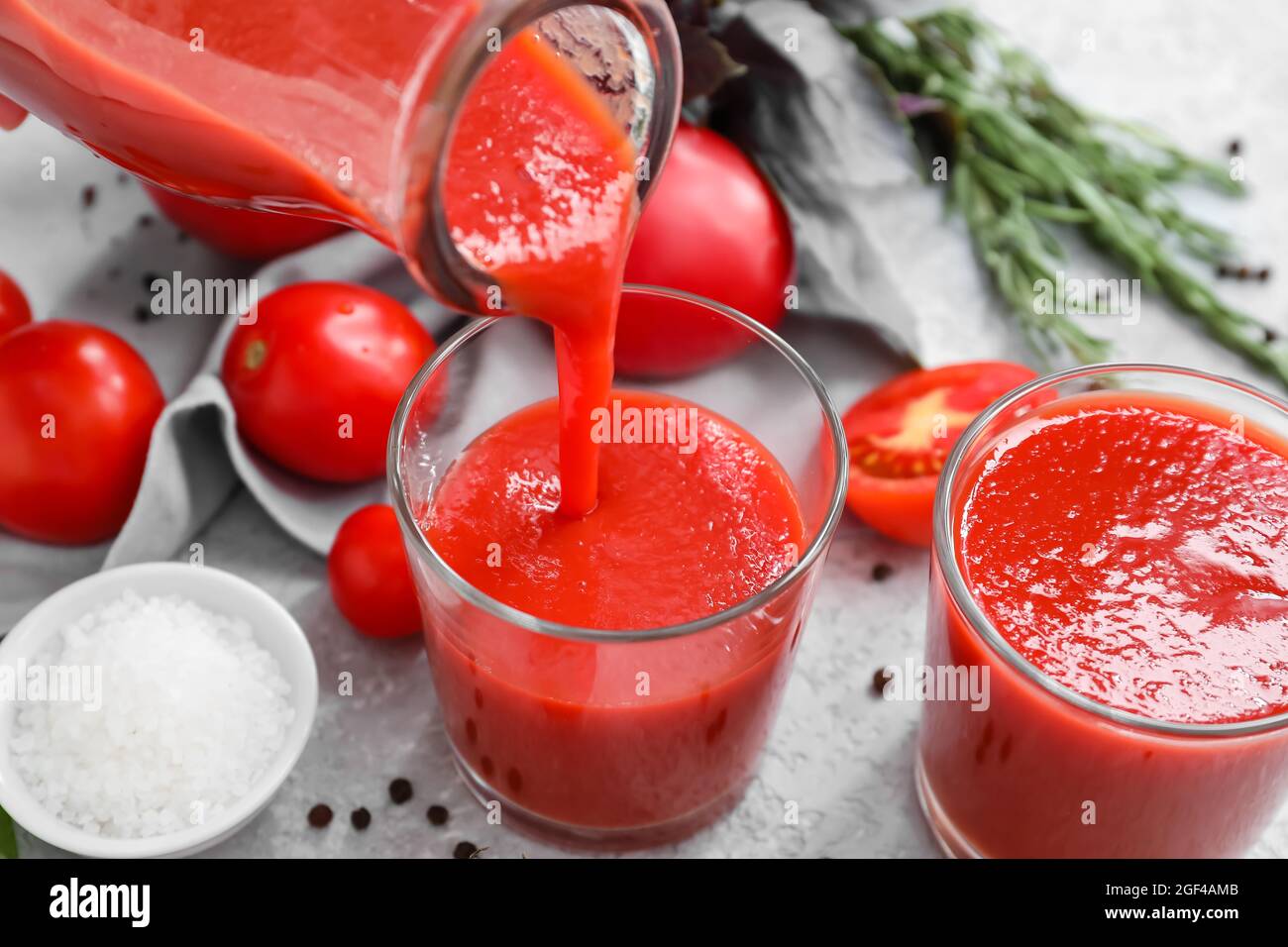 Pouring tasty tomato juice from bottle into glass on light background ...