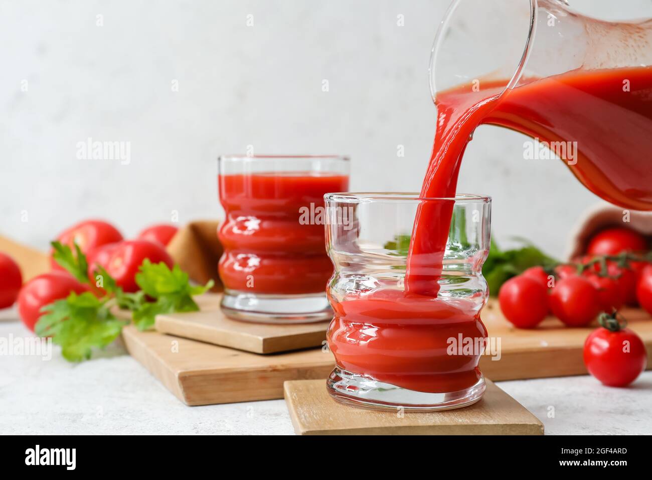Pouring tasty tomato juice from jug into glass on light background ...