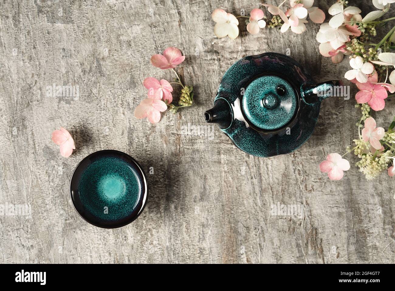 Green tea in dark turquoise clay teapot and small cup on grey wooden ...