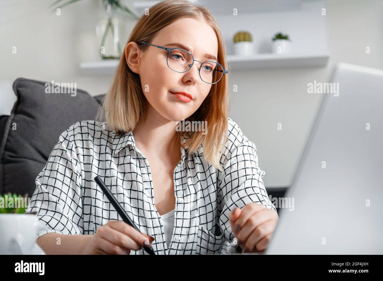Confident Blonde Woman In Glasses Working Using Laptop While Making Notes In Office Interior