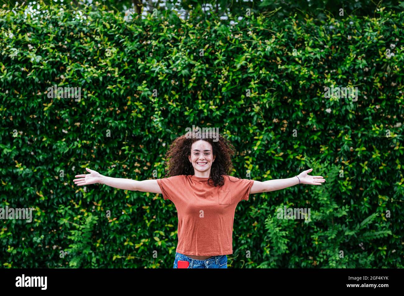 Happy young woman with arms outstretched in front of green ivy plants ...