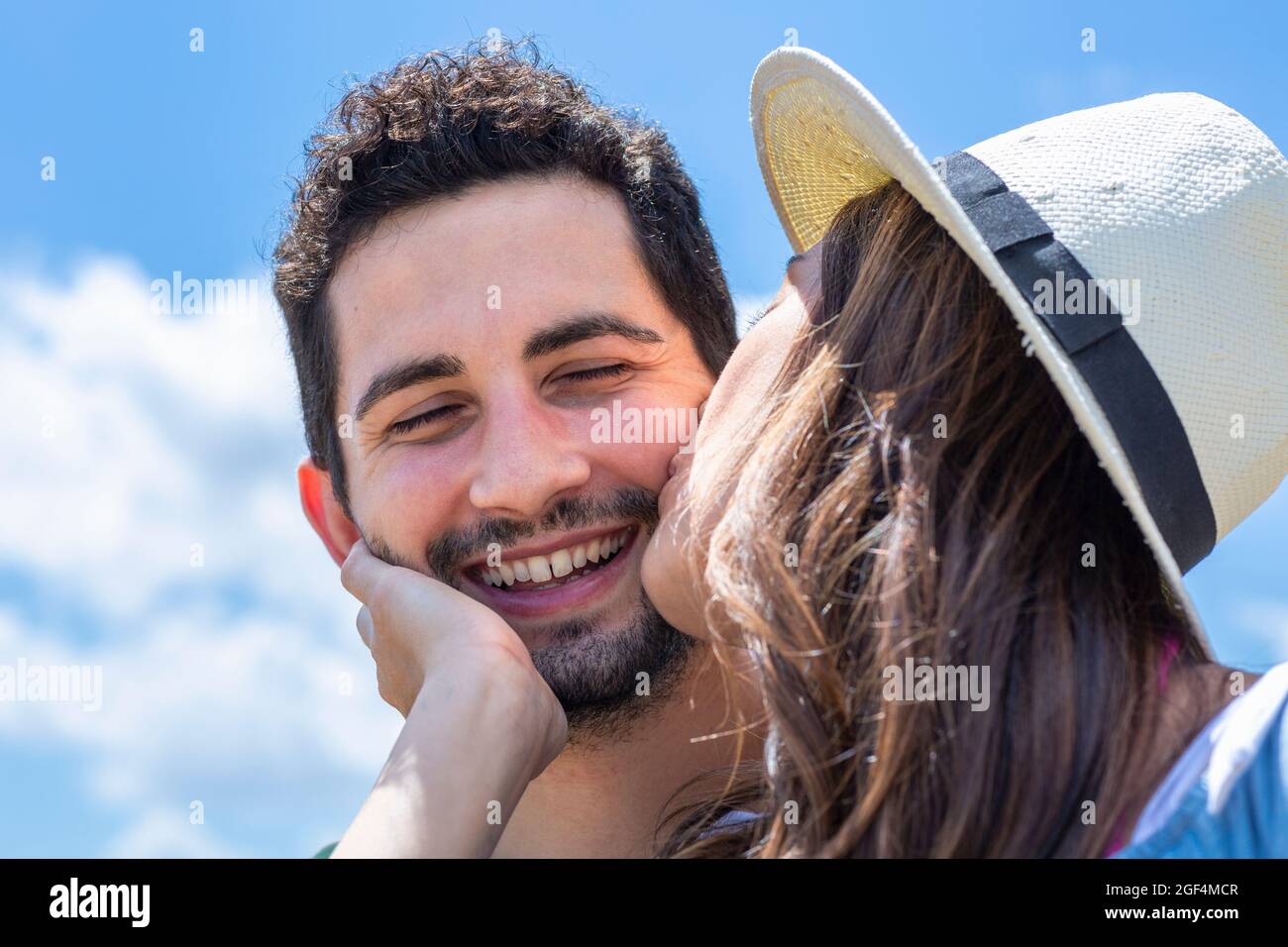 Girlfriend with hat kissing boyfriend during sunny day Stock Photo - Alamy