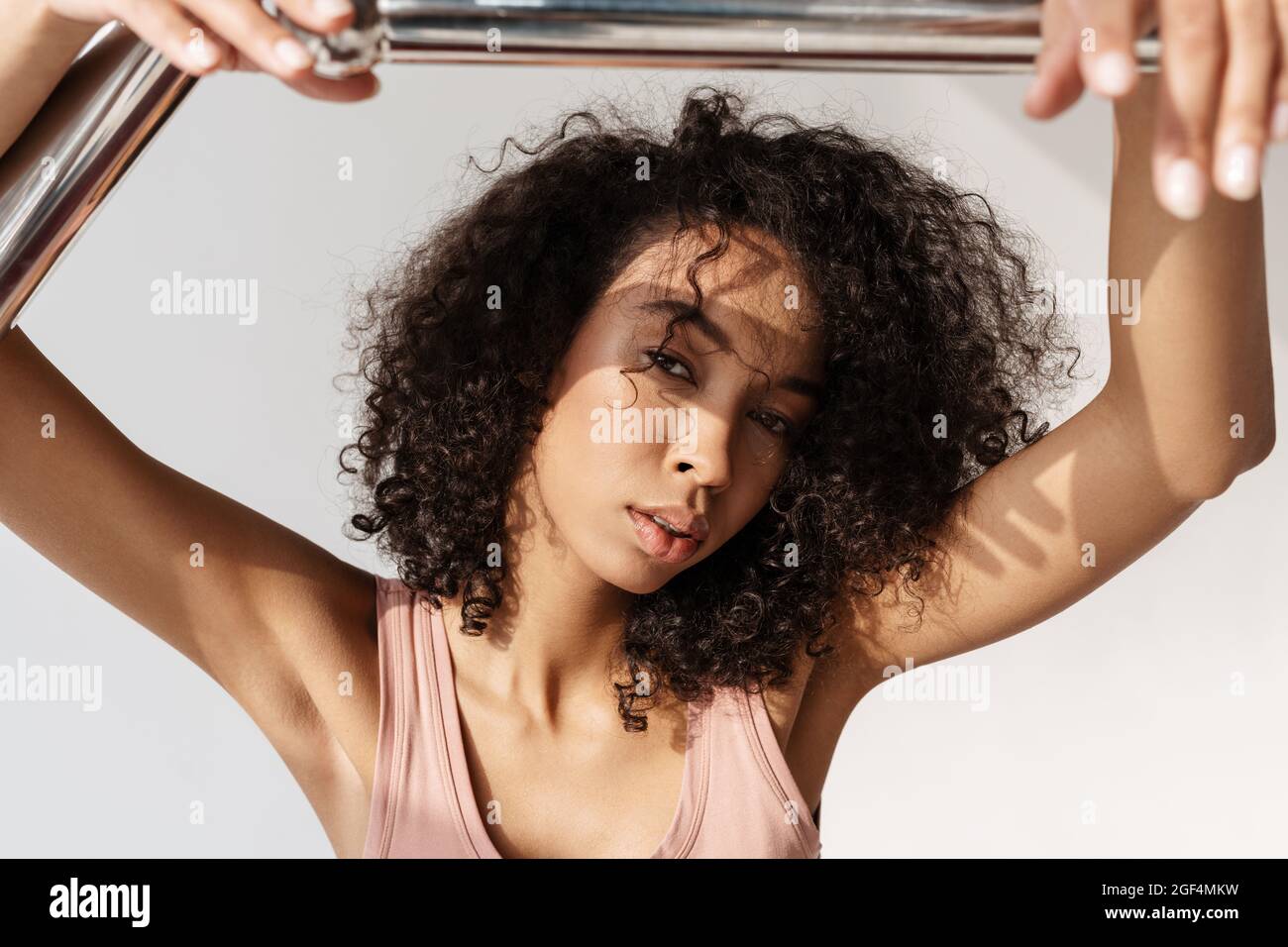 Young African Woman Wearing Brassiere Posing With Clothes Rail Isolated Over White Wall Stock