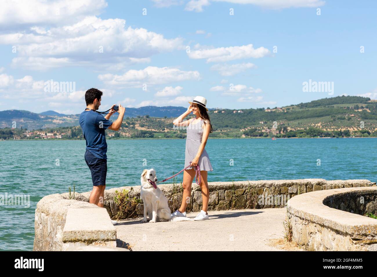 Boyfriend photographing girlfriend standing with dog on pier Stock ...