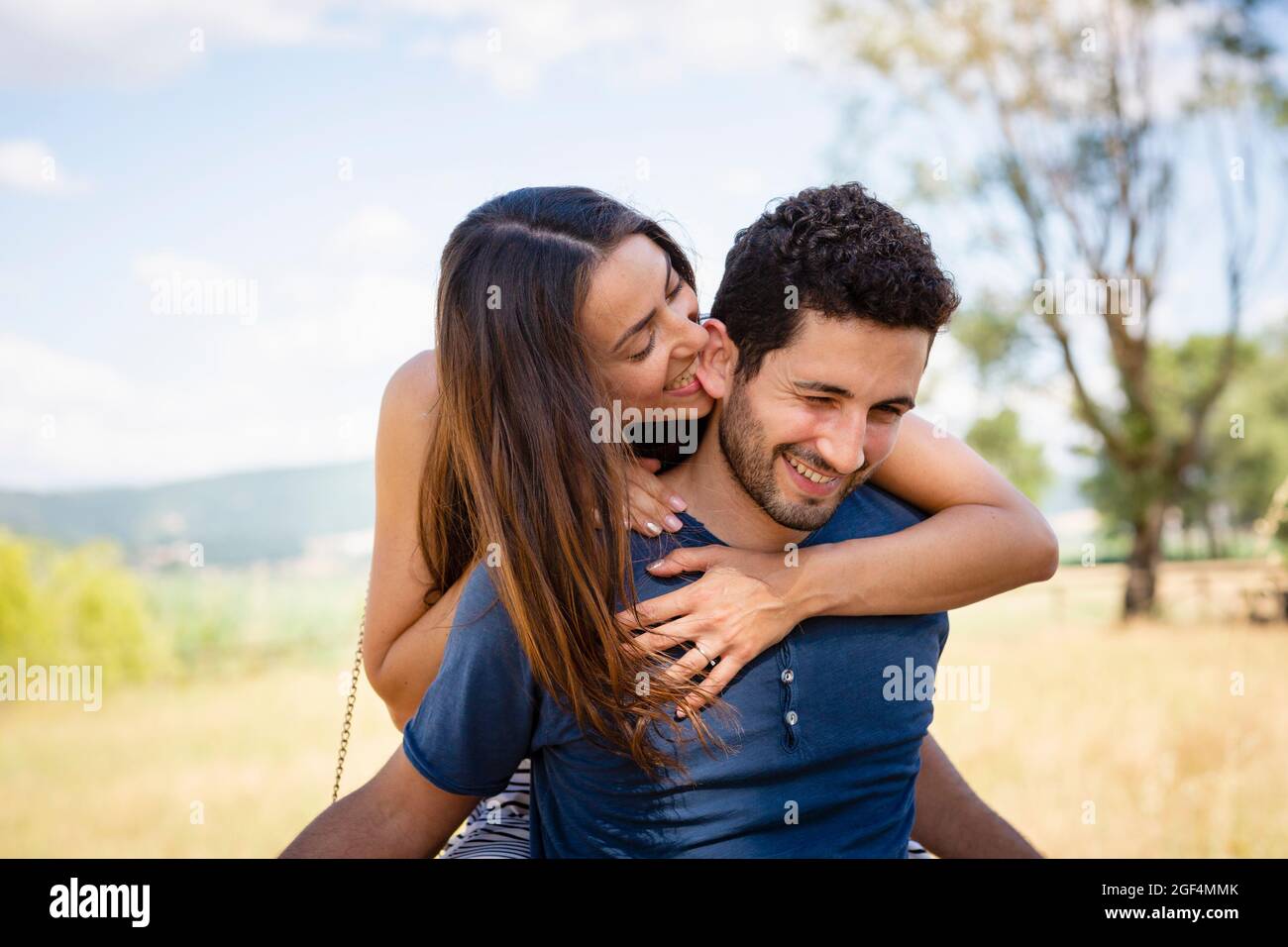 Playful woman biting boyfriend's ear while enjoying piggyback ride ...